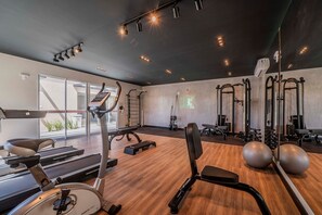 Academia com equipamentos de cardio, pesos livres e espelho grande.