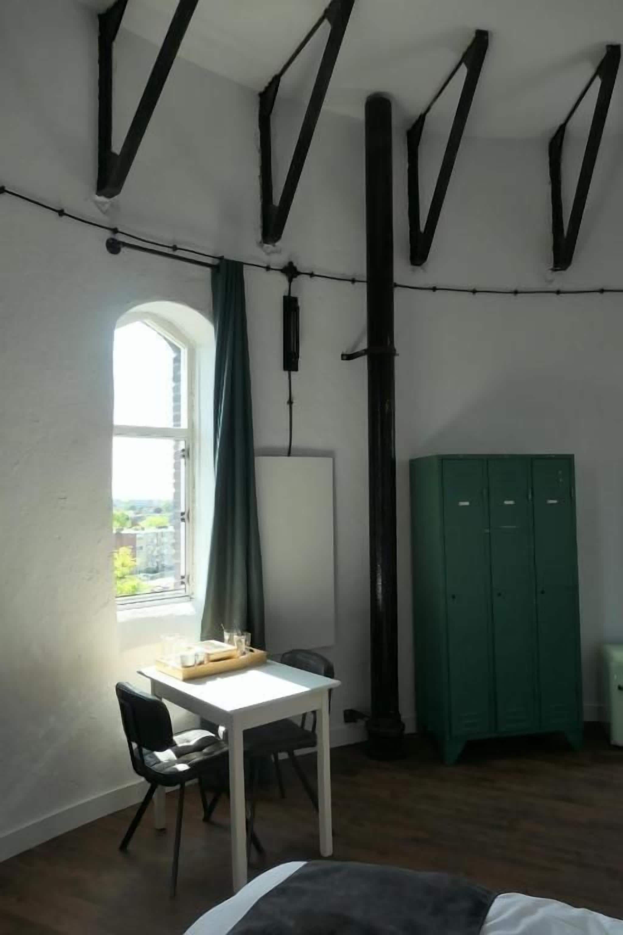 Quarto com cama, escrivaninha, cadeira, janela com cortinas e guarda-roupa verde.