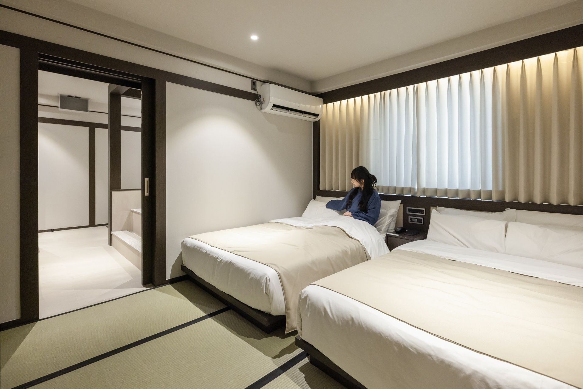 Quarto de hotel com duas camas, porta de correr, ar condicionado e janela com cortinas.