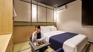 Quarto de hotel com cama, mesa de cabeceira e uma pessoa sentada à mesa.