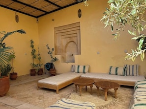Quarto com sofá, duas mesas de madeira, colchão e plantas em vasos.