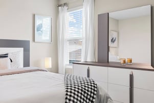Quarto moderno com cama, luminária de cabeceira e um espelho grande.