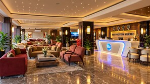 Um saguão moderno de hotel com balcão de recepção, área de estar e uma grande tela de televisão.