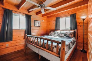 Um quarto de cabana de madeira, com uma cama, um ventilador de teto e um abajur.