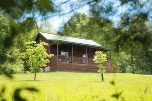 Uma cabana com varanda, cercada por árvores e grama.