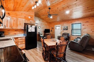 Interior de cabana com cozinha, área de refeições e espaço para sentar.