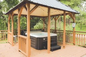 Um gazebo de madeira com banheira de hidromassagem, rodeado por um deck de madeira e um telhado de metal.