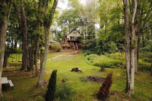 Uma cabana rodeada por uma floresta densa, com um caminho aberto que leva à entrada.