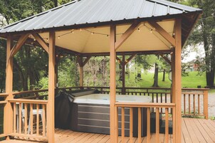 Um gazebo de madeira com hidromassagem, cercado por um deck e árvores.