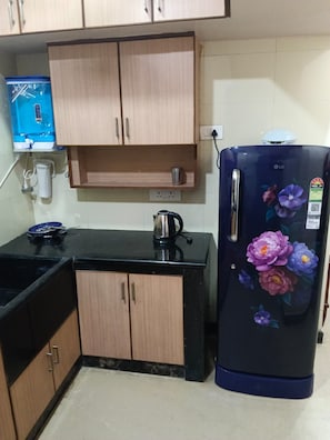 Cozinha com armários de madeira, bancada preta, chaleira e geladeira com detalhes florais.