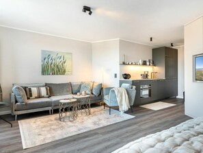 Uma sala de estar moderna com um sofá cinzento, uma mesa redonda pequena e um quadro na parede.