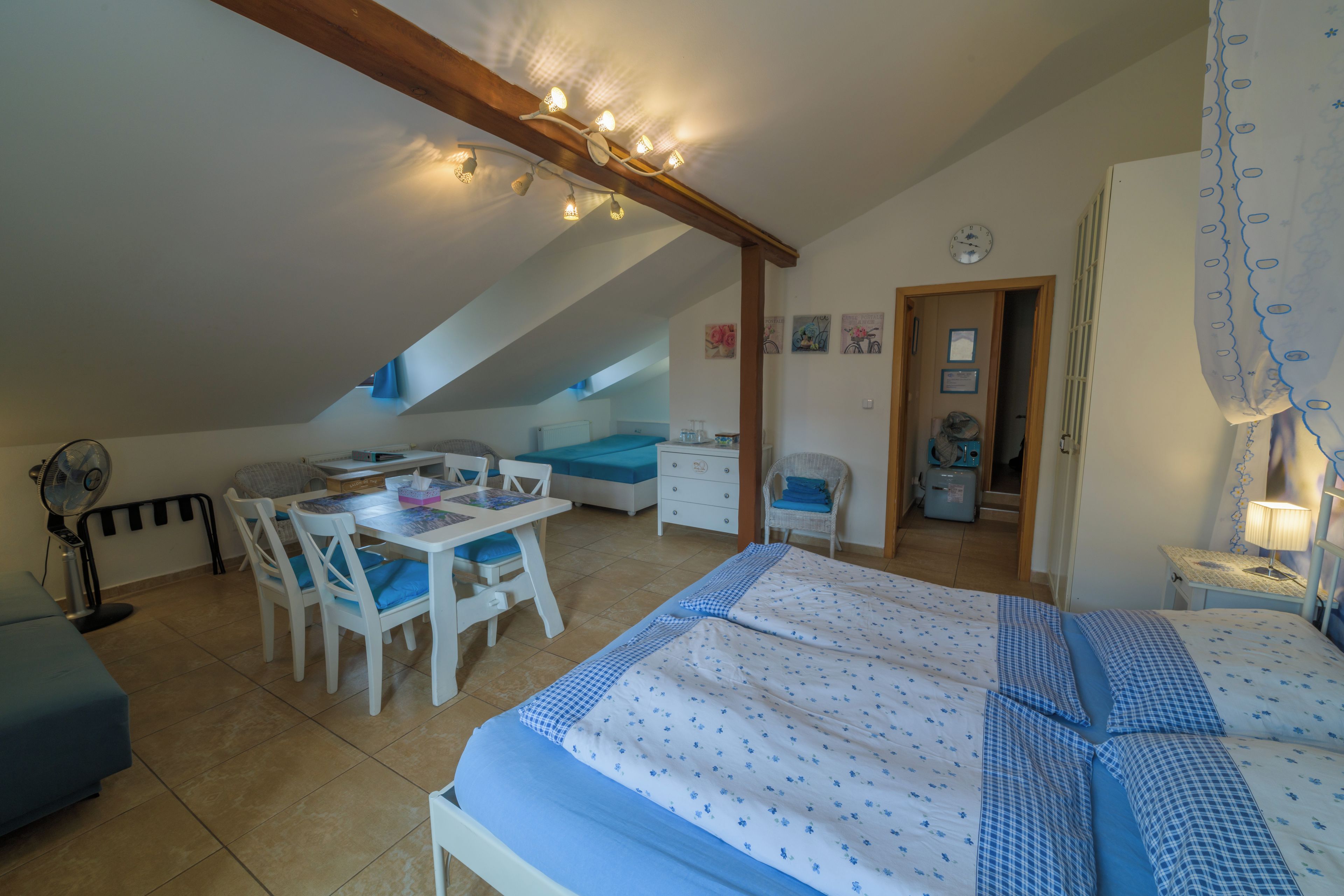 Quarto com cama, mesa, cadeiras, ventoinha e janela.