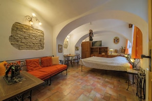 Quarto aconchegante com parede de pedra, uma cama, um sofá, uma mesa com abajur e uma televisão.