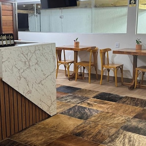 Interior de restaurante com balcão de mármore, cadeiras de madeira e piso estampado.