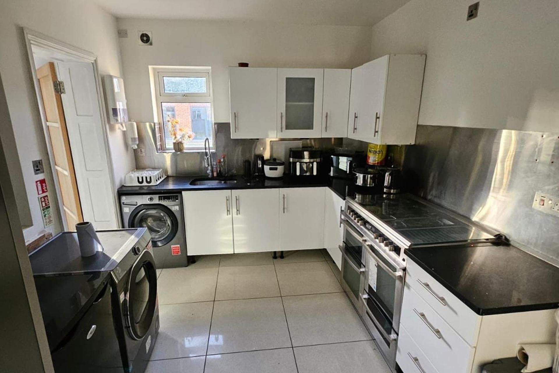 Cozinha compacta com armários brancos, máquina de lavar, fogão e pia.