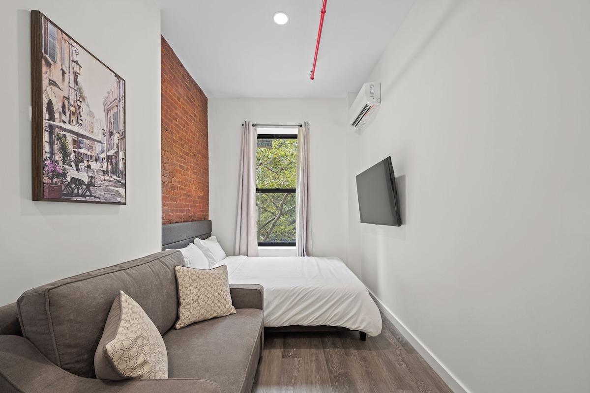Quarto moderno com cama, sofá, televisão e janela com cortinas.