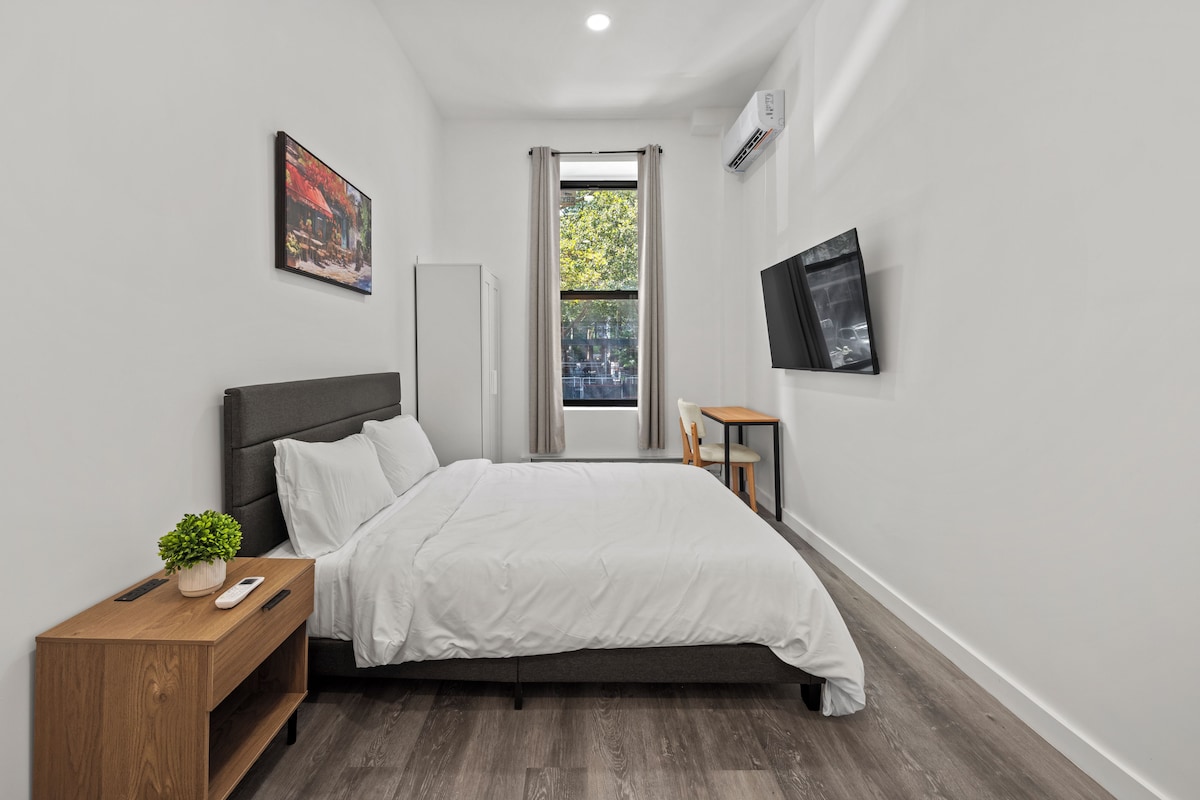 Quarto moderno com cama, mesa de cabeceira e uma pequena mesa com cadeira.