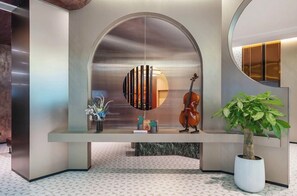 Uma área de recepção com design moderno, destacando uma parede curva, uma vitrine de vidro com um violino e um vaso de planta.