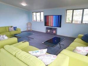 Uma sala de estar com sofás verdes, uma TV de tela plana e uma estante de livros.