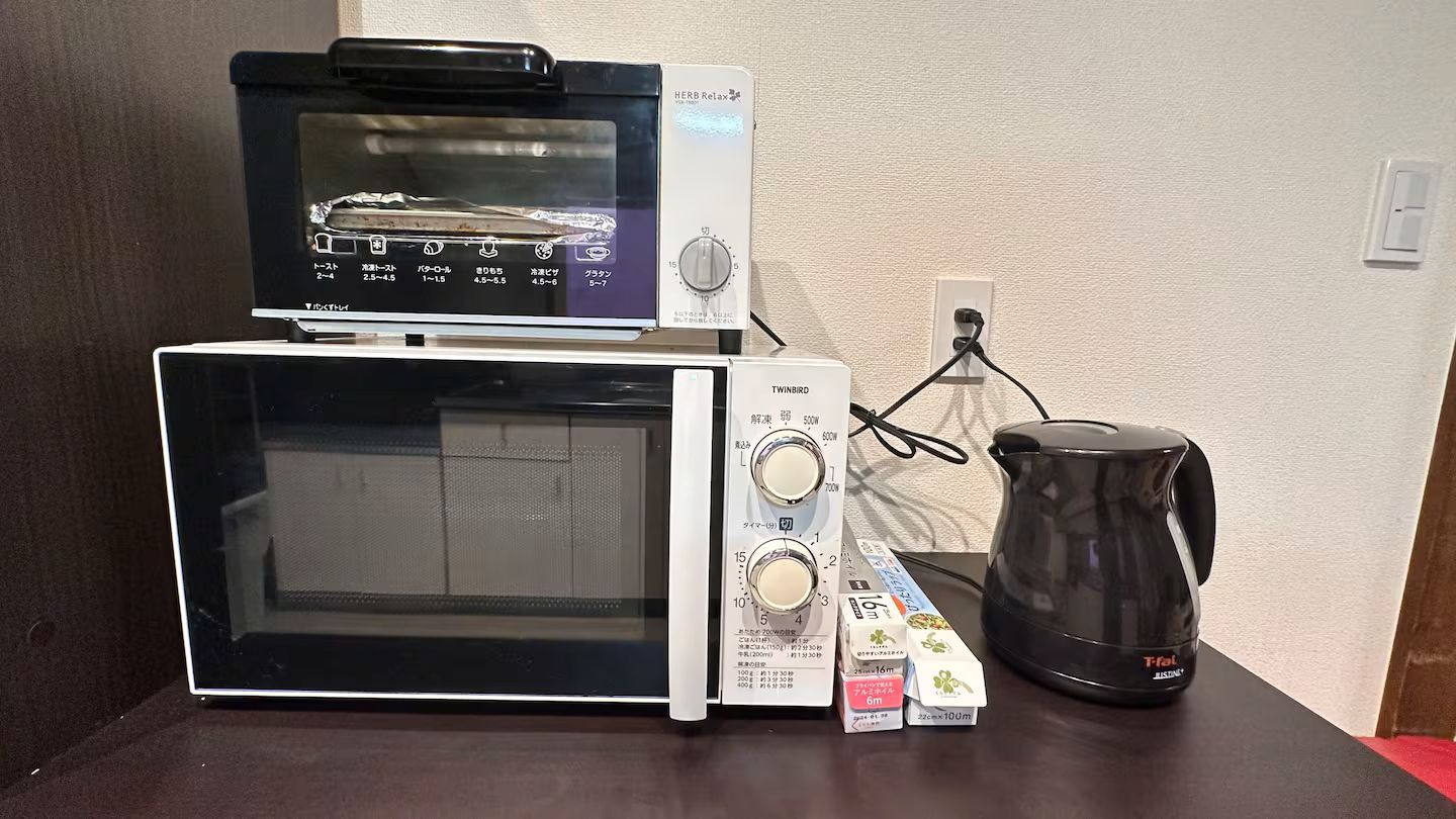 Um forno de micro-ondas com visor digital, uma cafeteira e uma caixa de chá sobre uma mesa.