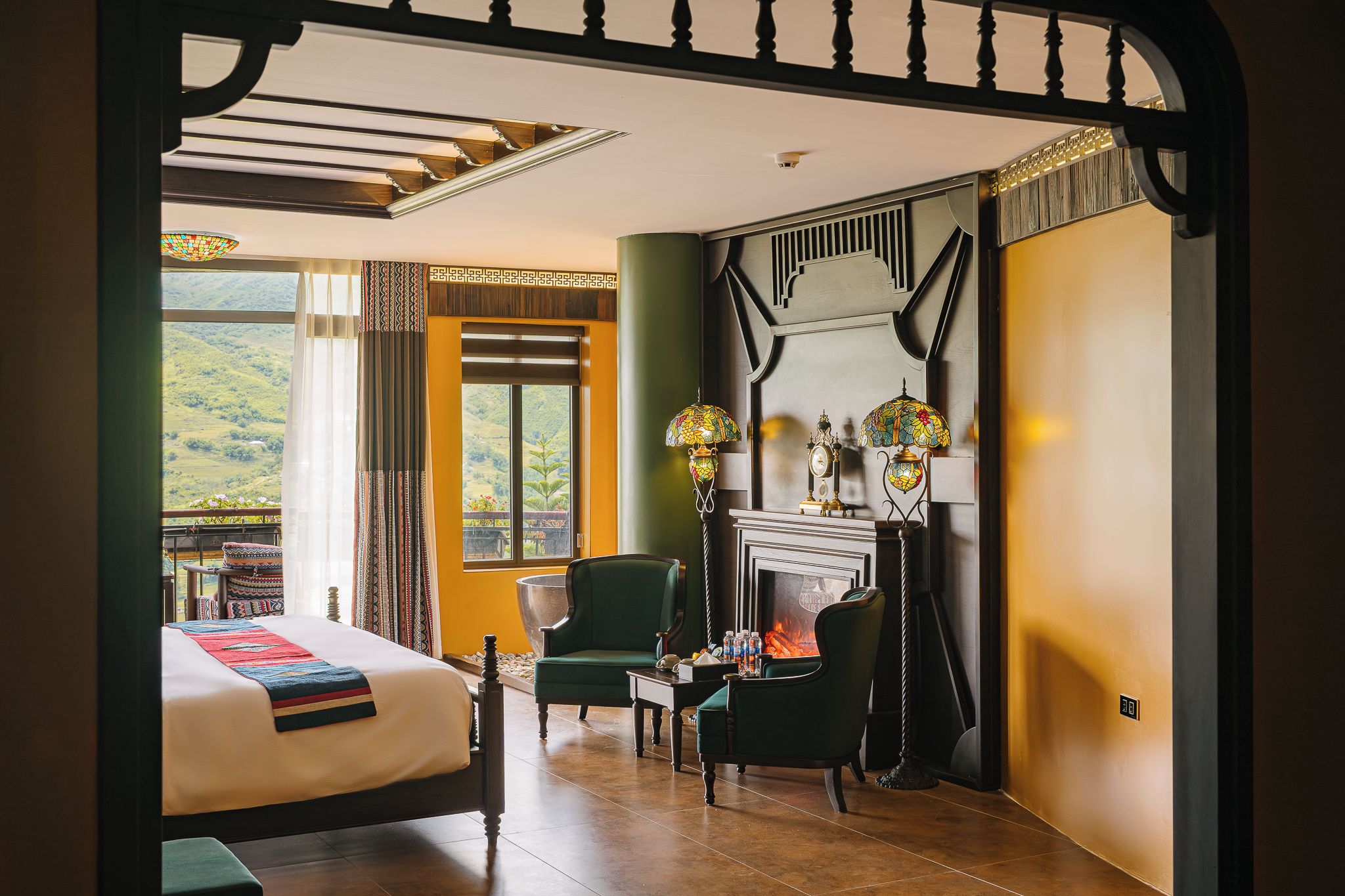 Quarto de hotel com cama, duas cadeiras, lareira e vista para o exterior.