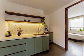 Cozinha moderna com bancada de mármore, pia embutida e prateleira de madeira acima.