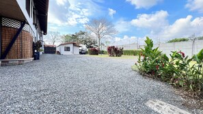 Uma entrada de cascalho leva a um edifício com telhado vermelho, um pequeno galpão e uma árvore.