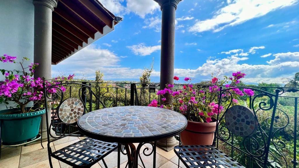 Um pátio com mesa redonda e cadeiras, rodeado por plantas em vasos e vista para a paisagem.