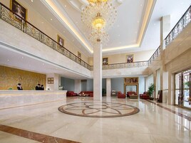 Um hall espaçoso com um design circular central no chão, um lustre imponente e um balcão de recepção.