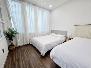 Quarto de hotel com duas camas, um vaso de planta e uma janela com cortinas.