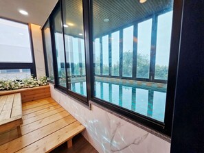 Um banco de madeira e uma janela ampla com vista para uma piscina e árvores.