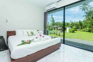 Quarto moderno com cama grande, vista para um jardim exuberante e porta de vidro deslizante.