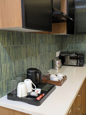 Cozinha com micro-ondas, cafeteira e bandeja com chávenas e chaleira.