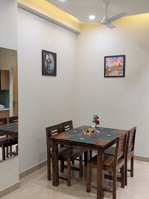Uma sala de jantar com mesa e cadeiras, um ventilador de teto e duas obras de arte emolduradas nas paredes.