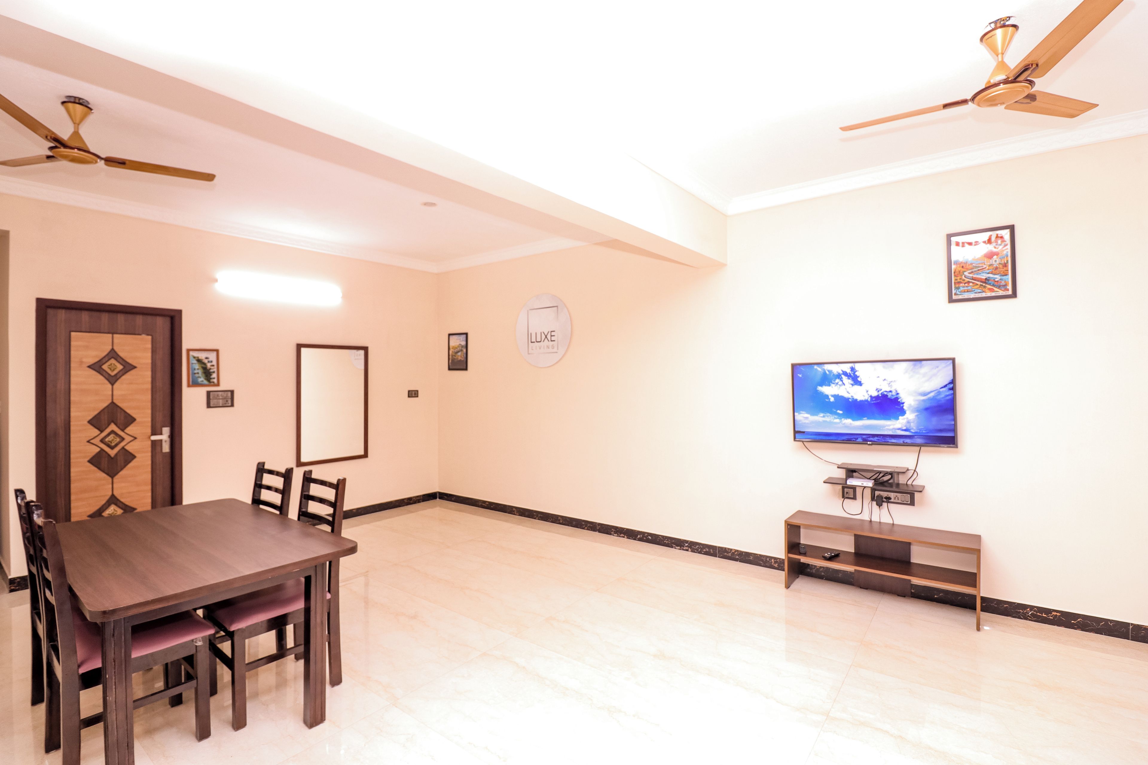 Uma área de jantar com mesa e cadeiras, um ventilador de teto, uma televisão sobre um suporte e uma parede com relógio e quadros.
