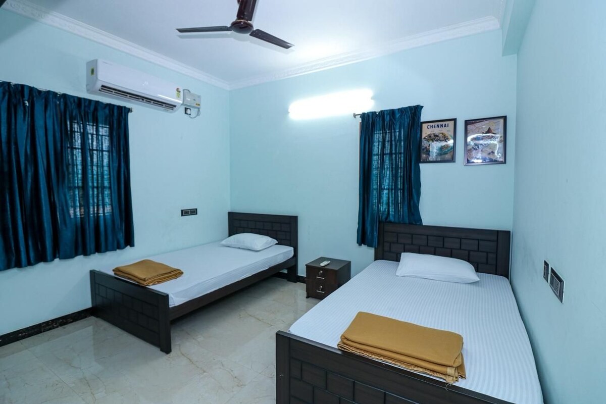 Quarto com duas camas de solteiro, ventilador de teto, ar condicionado e duas fotos emolduradas na parede.
