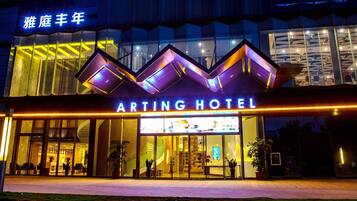 Exterior do ARTING HOTEL com design moderno, destacando um letreiro de neon e fachada de vidro.