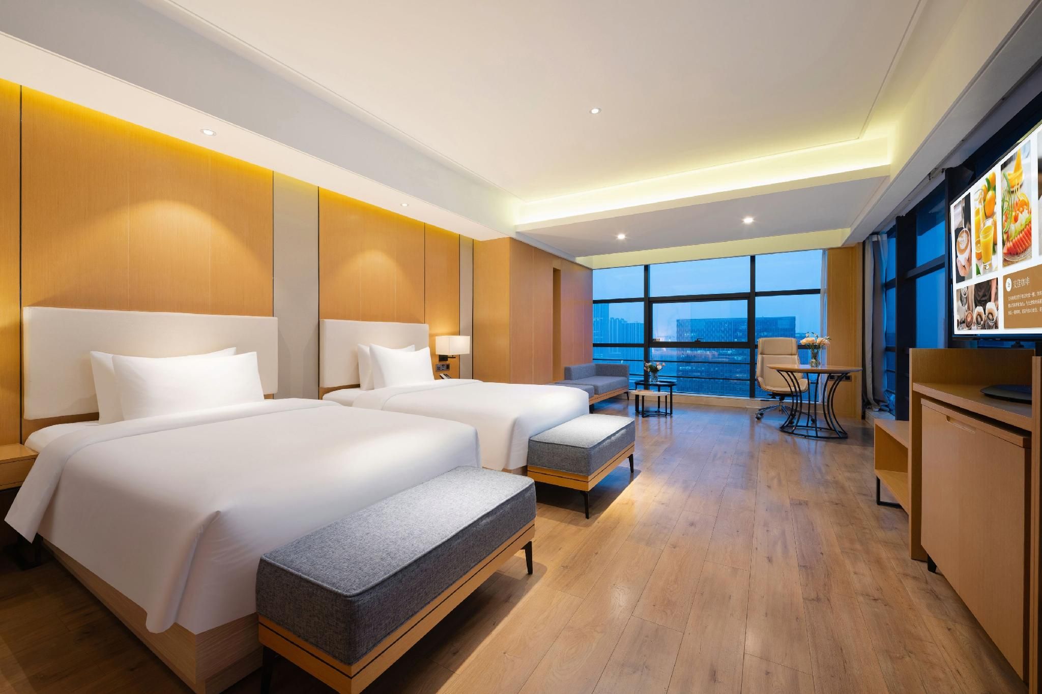 Quarto de hotel com duas camas, um espaço de estar e uma grande janela com vista para a cidade.