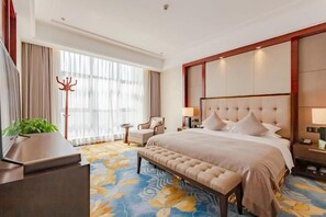 Quarto de hotel com uma cama grande, escrivaninha, cadeira e janela com cortinas.