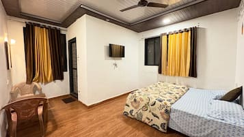 Quarto com cama, escrivaninha, cadeira, televisão e ventoinha no teto.