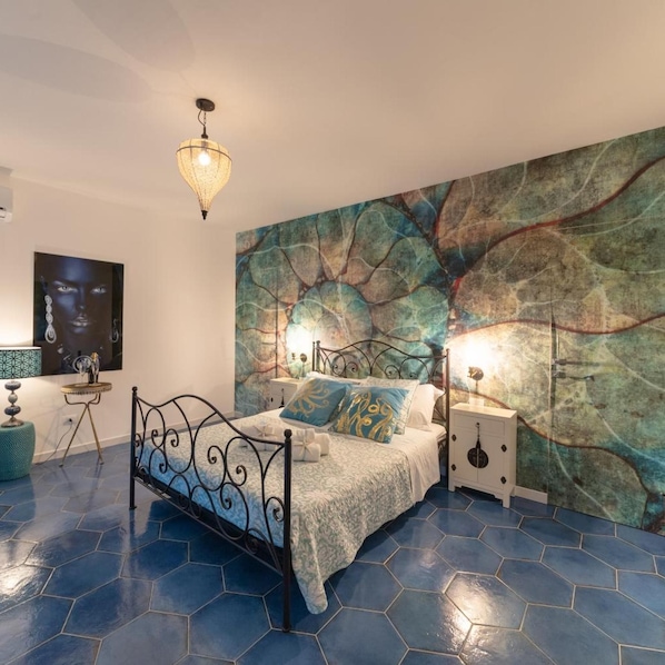 Quarto com cama, um mural na parede, luminária pendente e mesa de cabeceira.