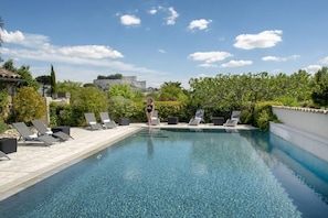 Piscina com espreguiçadeiras e uma pessoa próxima à borda.