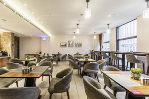 Interior de restaurante moderno com várias mesas e cadeiras, iluminação pendente e quadros nas paredes.