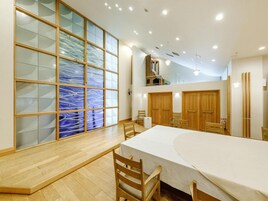 Um quarto amplo com uma grande mesa de jantar, cadeiras de madeira, uma escada e vista através de uma divisória de vidro.
