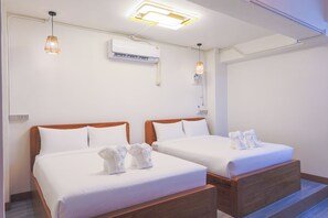 Quarto de hotel com duas camas, roupa de cama branca, ventoinha no teto, ar condicionado e luminária de cabeceira.
