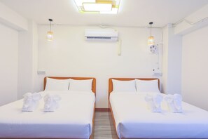 Quarto de hotel com duas camas, ventilador de teto, ar condicionado e luminária fixada na parede.