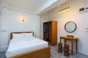 Quarto de hotel com cama, guarda-roupa de madeira, espelho redondo e pequena mesa de madeira.