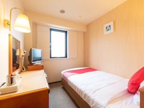 Quarto de hotel com cama, escrivaninha com luminária, televisão e janela.