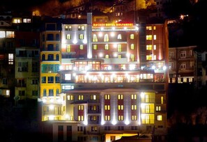 Hotel de vários andares com janelas e varandas iluminadas, exibindo uma placa grande no topo.