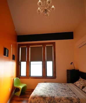 Quarto com cama, janela, cadeira verde e cômoda.